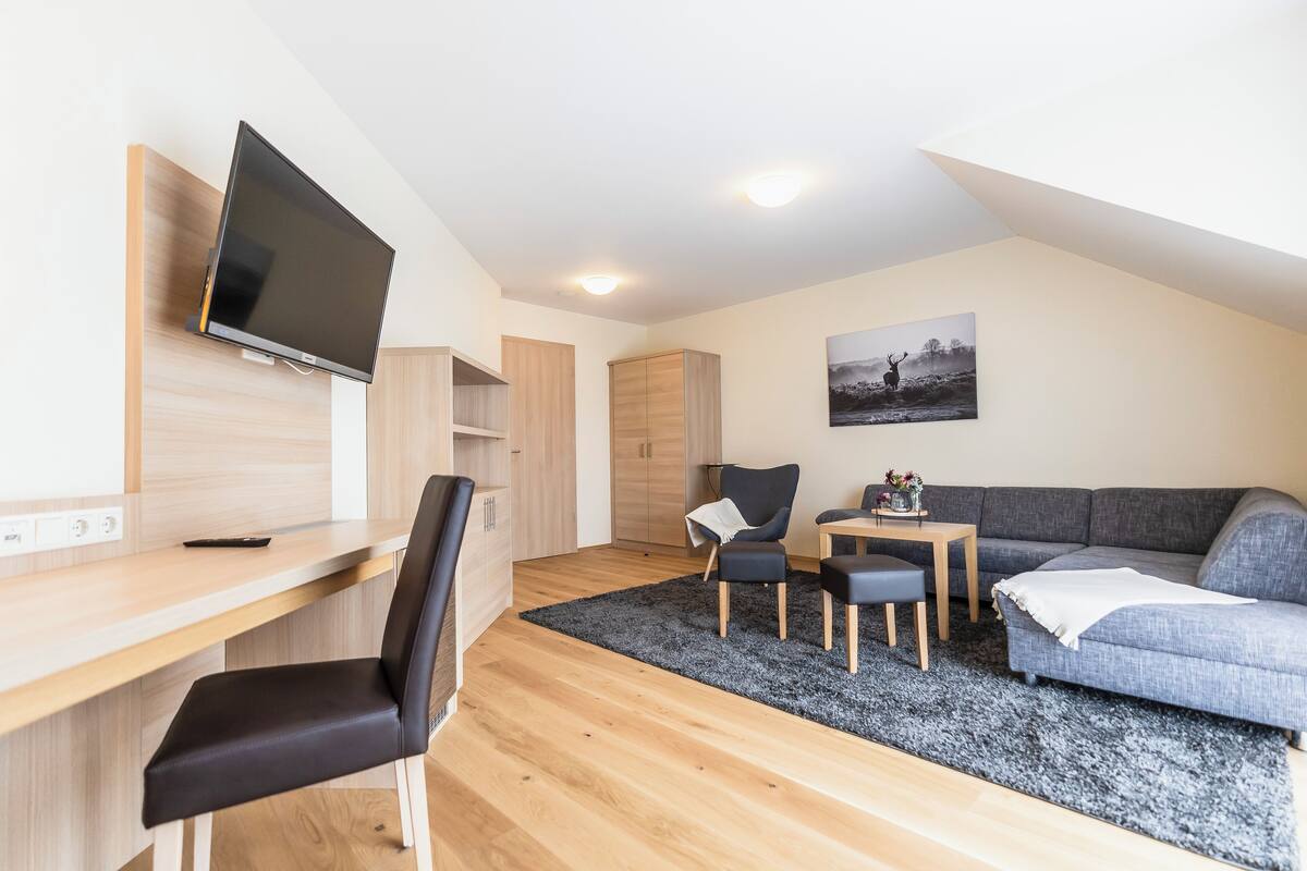 Uma sala de estar moderna com televisão de tela plana, móveis de madeira, um sofá cinza e um tapete preto.