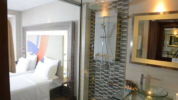 Um banheiro moderno com chuveiro em box de vidro, pia de vidro e cama com roupa de cama branca.