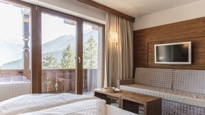 Quarto de hotel com cama, sofá, televisão na parede e vista para as montanhas pela janela.
