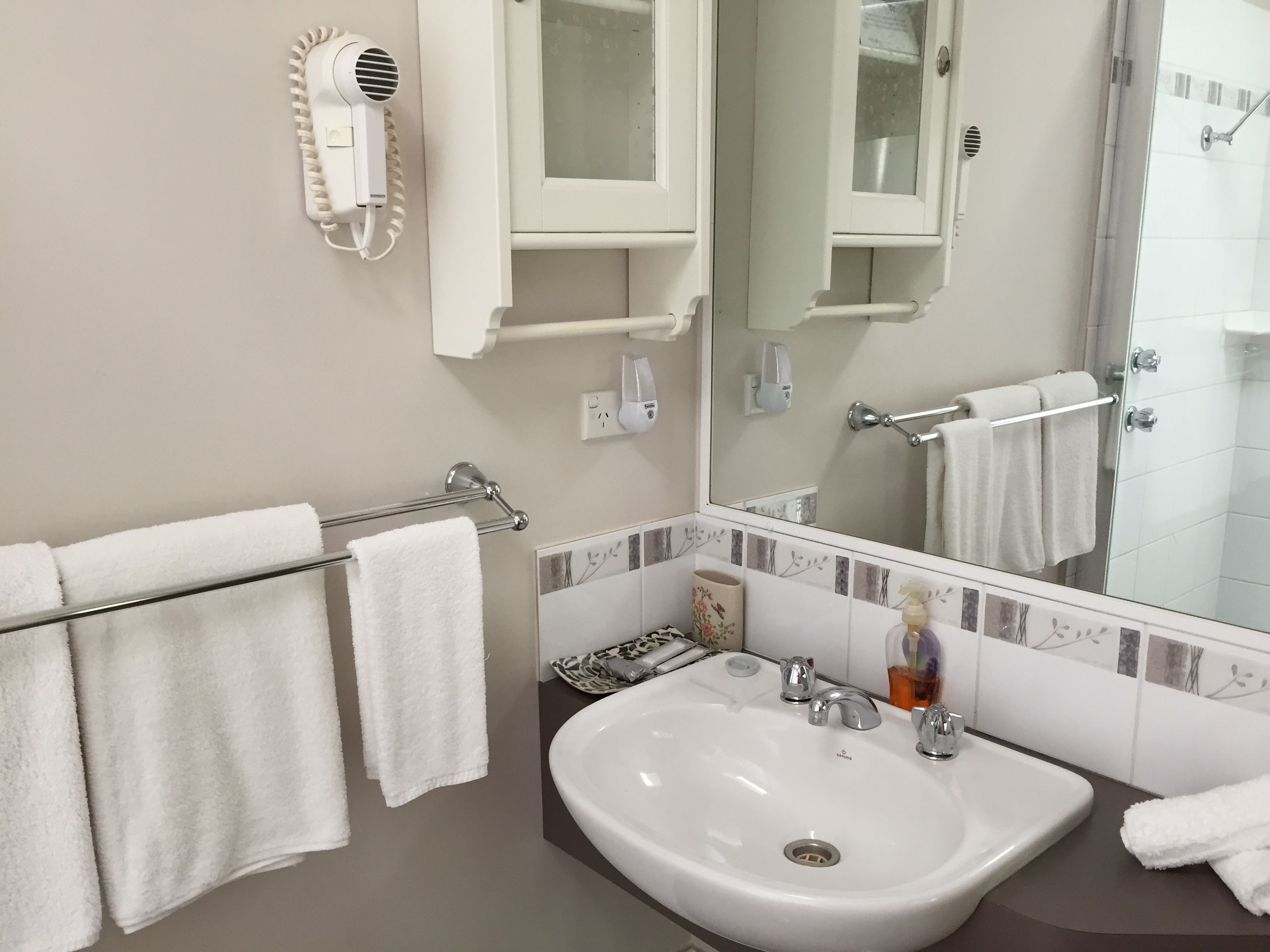 Uma casa de banho moderna com uma pia branca, um secador de cabelo, um espelho e um porta-toalhas.