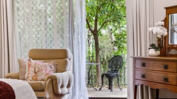 Quarto com cama, cadeira, cômoda e vista para uma árvore através da janela.
