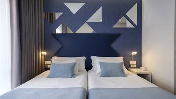 Uma cama de casal com duas almofadas, uma mesa de cabeceira com abajur e um design geométrico na parede.