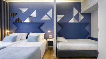 Quarto de hotel com duas camas, uma mesinha de cabeceira e decorações geométricas nas paredes.