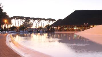 Área de piscina com espreguiçadeiras e um bar ao fundo.