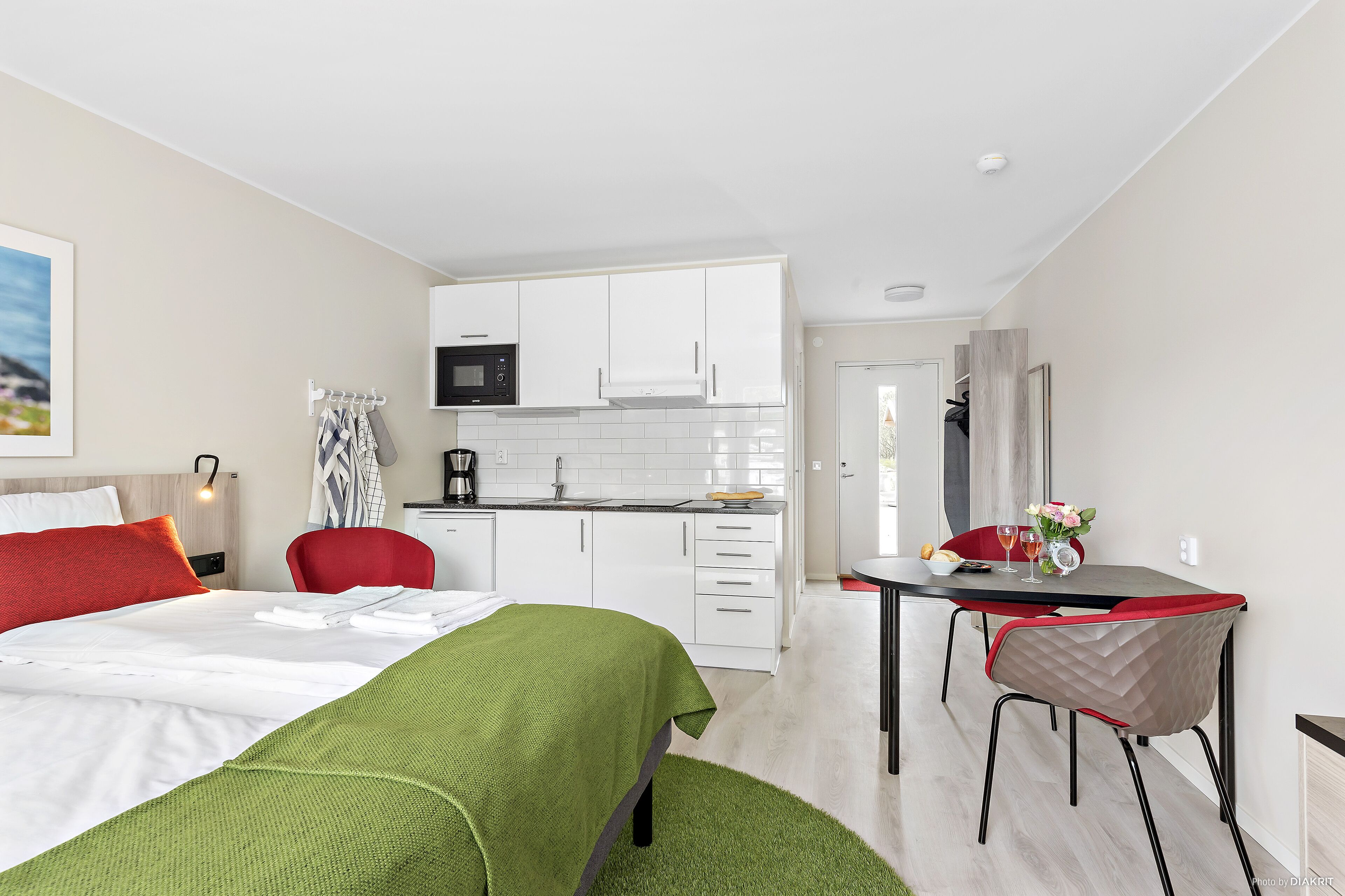Quarto de hotel moderno com cama, escrivaninha, cadeira, cozinha compacta e banheiro.