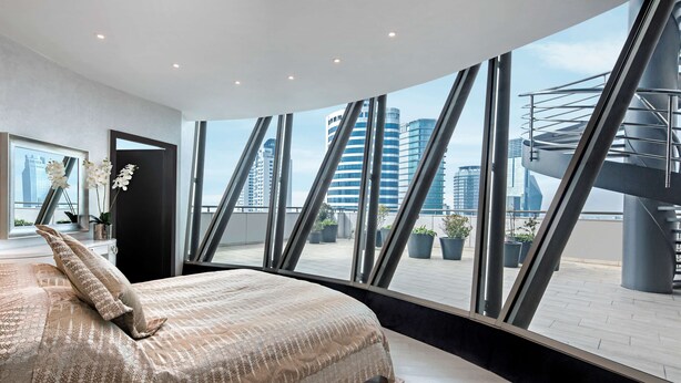 Quarto moderno com uma cama grande, vista para a cidade através de janelas do chão ao teto e uma escada do lado de fora.