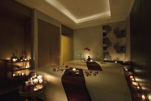 Um quarto de spa com duas camas, velas e uma pequena mesa com um porta-flores.