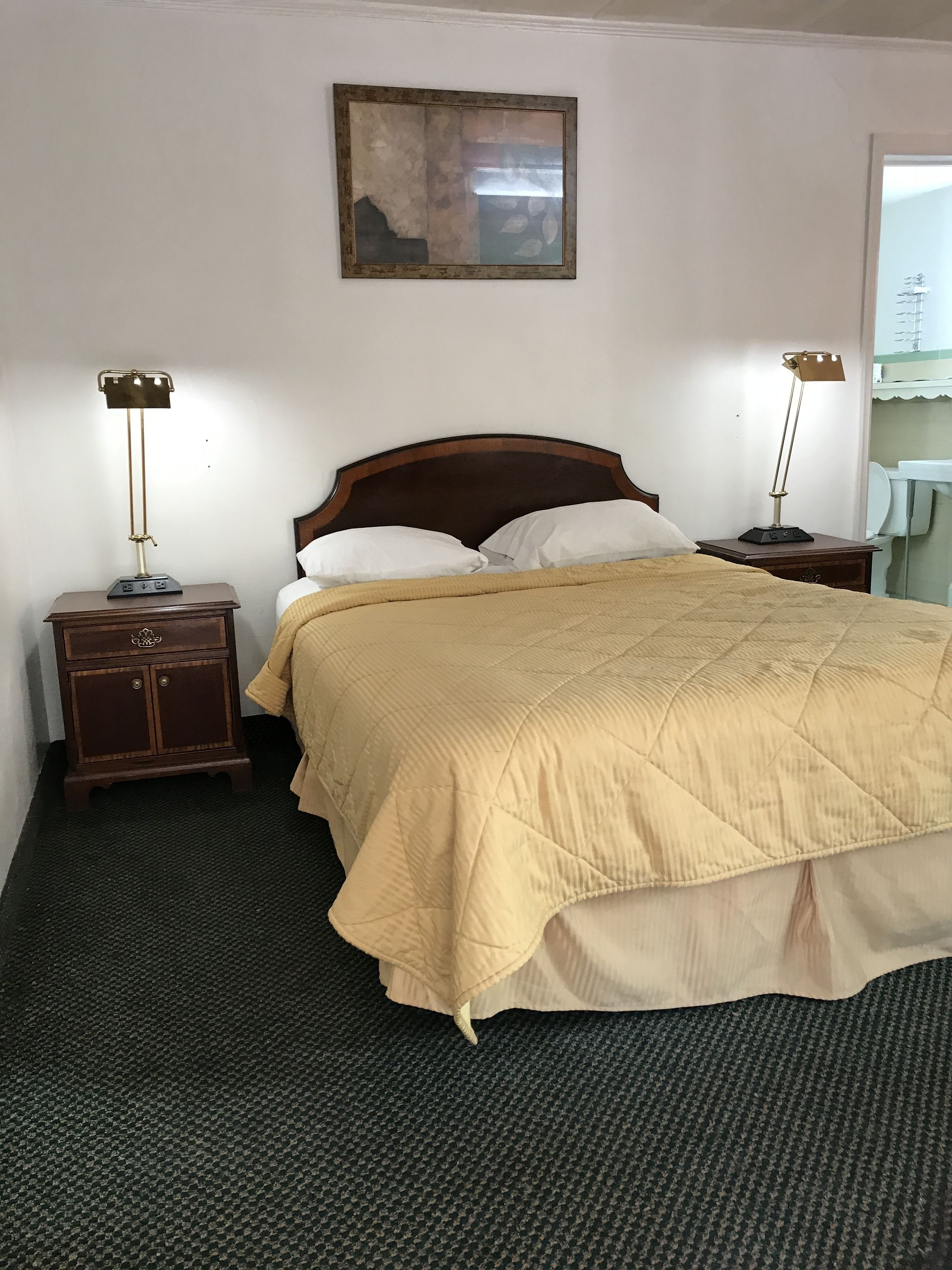 Cama bem arrumada com um edredom acolchoado, duas mesas de cabeceira com abajures, uma cabeceira de madeira e um quadro na parede.