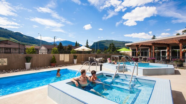 Uma área de piscina com várias piscinas, um espaço coberto com assentos e um cenário montanhoso ao fundo.