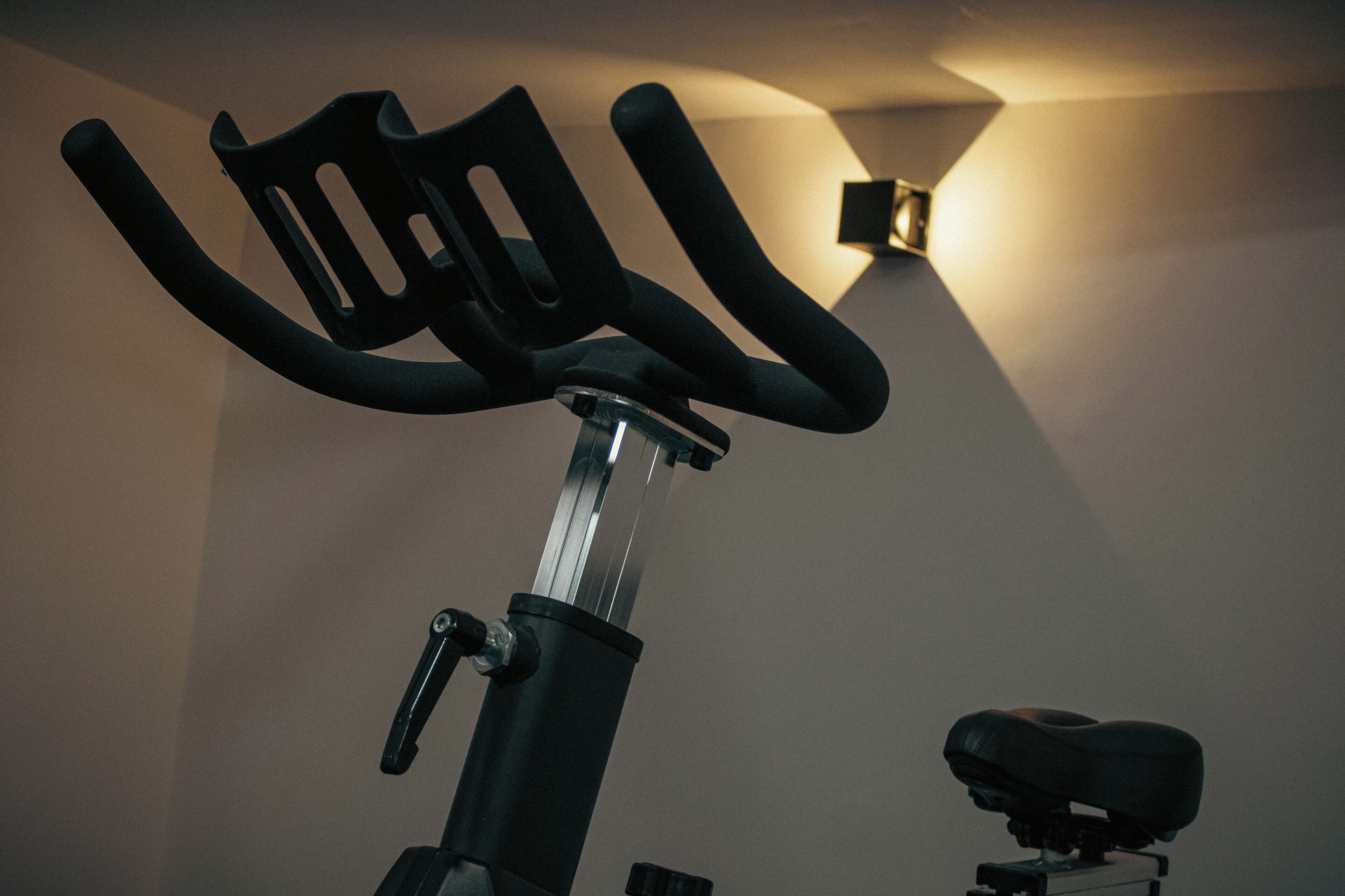 Uma bicicleta ergométrica fixa com painel de controle, um assento e um suporte de luz fixado na parede.