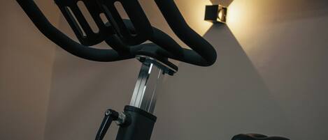 Uma bicicleta ergométrica fixa com painel de controle, um assento e um suporte de luz fixado na parede.