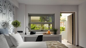 Quarto moderno com uma cama grande, uma escrivaninha com um laptop, uma janela com vista para vegetação e uma porta que dá para uma área externa.
