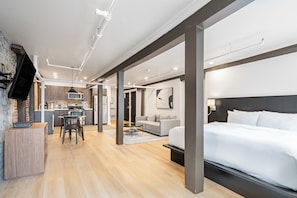 Quarto de hotel moderno com uma cama grande, área de refeições com mesa e cadeiras, cozinha e sala de estar com sofá.