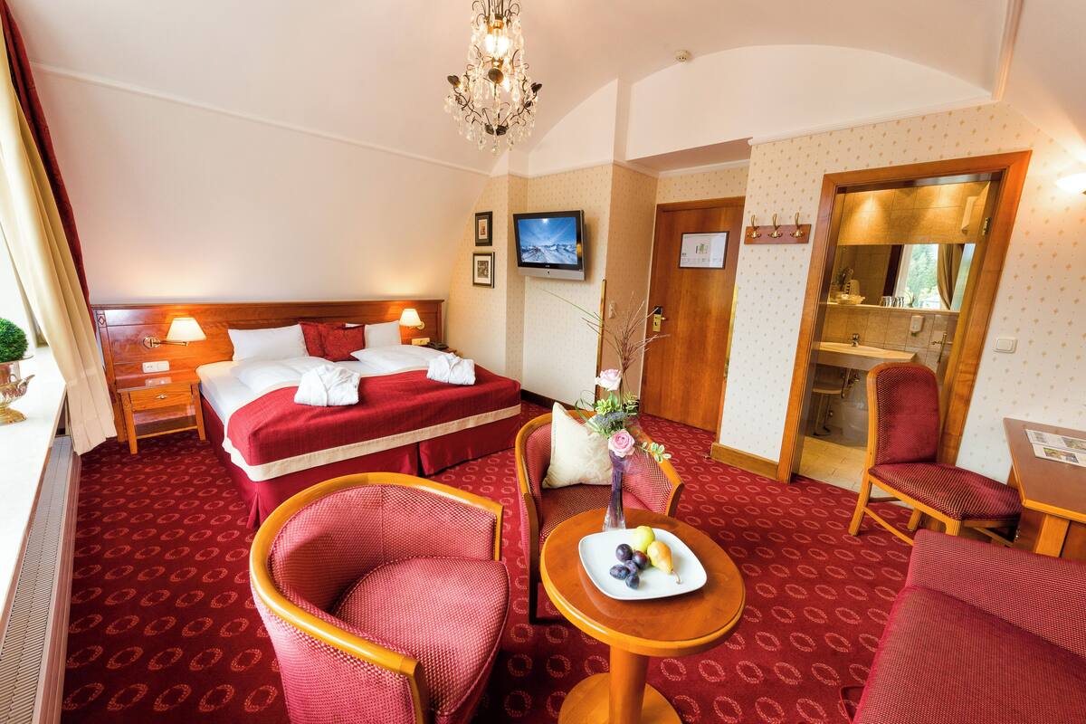 Quarto de hotel com cama, televisão, mesa de jantar com fruta e área de estar com cadeiras.
