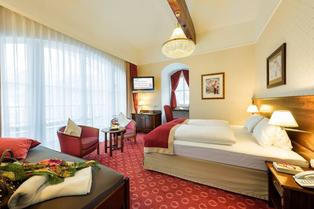 Quarto de hotel com duas camas, uma escrivaninha, uma cadeira, televisão e um candelabro.
