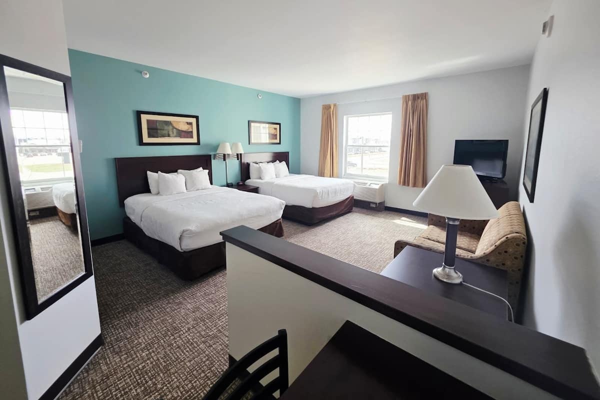 Quarto de hotel com duas camas, uma mesa, uma cadeira, uma televisão e uma janela com cortinas.