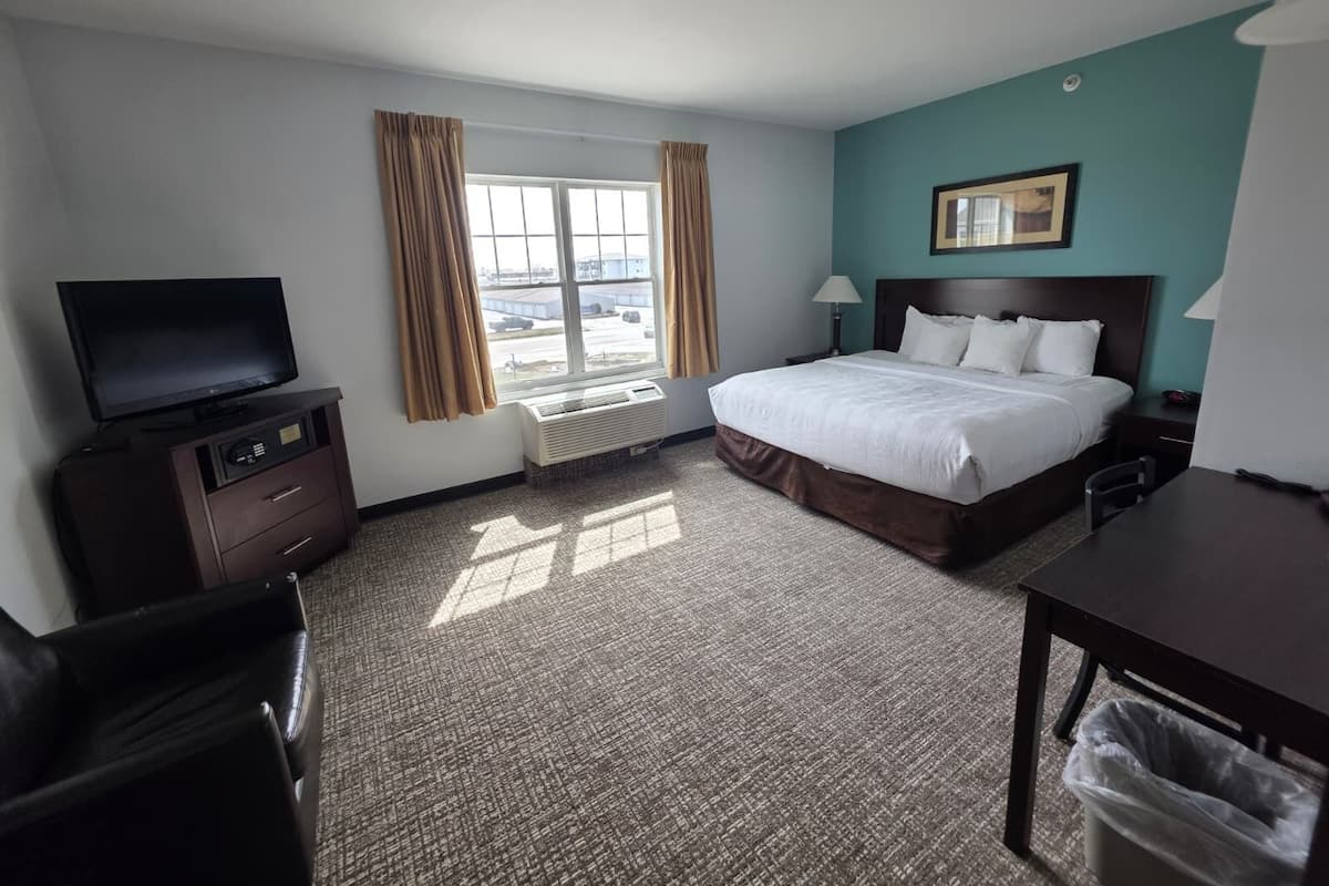 Quarto de hotel com cama, televisão em uma cômoda, escrivaninha, cadeira, janela com cortinas e vista para o exterior.