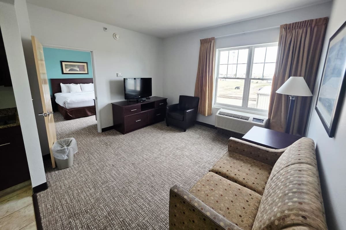 Quarto de hotel com cama, televisão, secretária, cadeira, sofá e janela com cortinas.