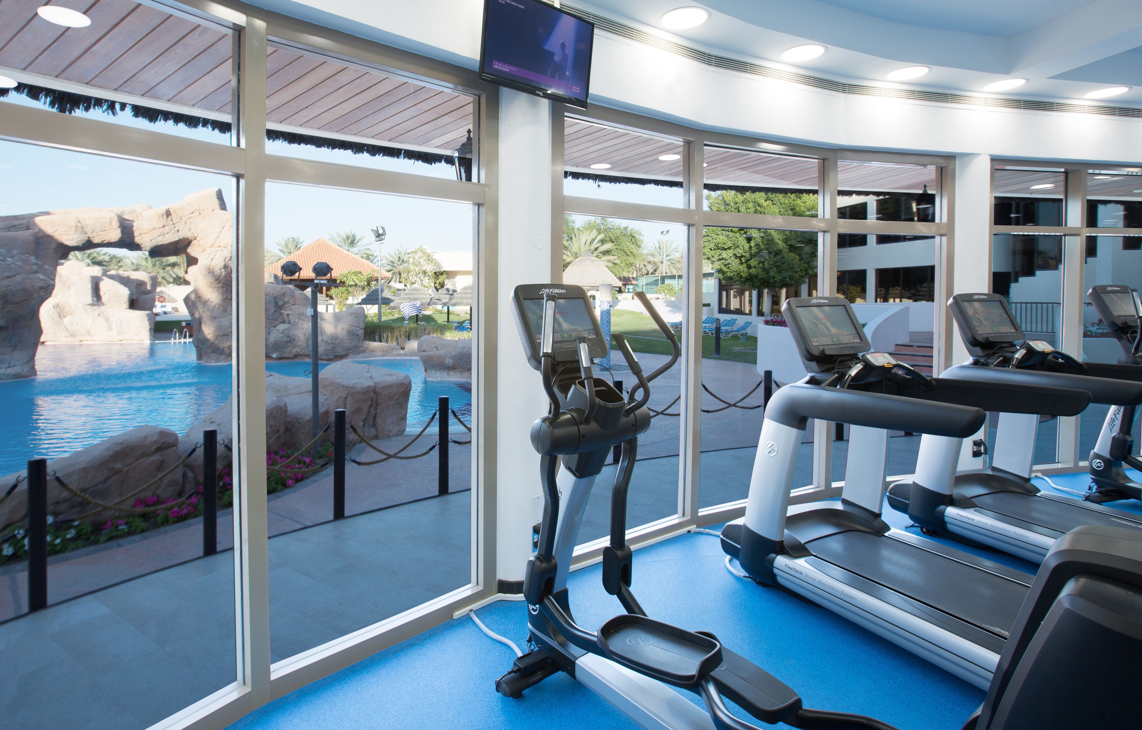 Centro de fitness com esteiras, elíptica e área de piscina visíveis por grandes janelas.