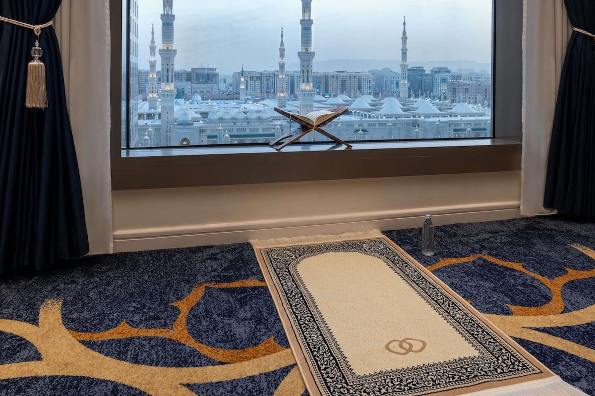 Quarto com vista para a paisagem urbana, um tapete de oração e um livro no parapeito da janela.