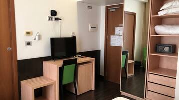 Quarto de hotel compacto com escrivaninha, cadeira e armário com espelho.