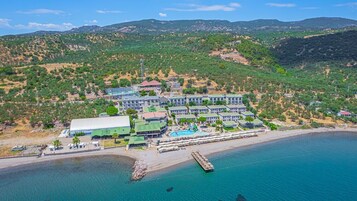 Vista aérea de um hotel à beira-mar, com vários edifícios, piscina e um píer que se projeta para o oceano.