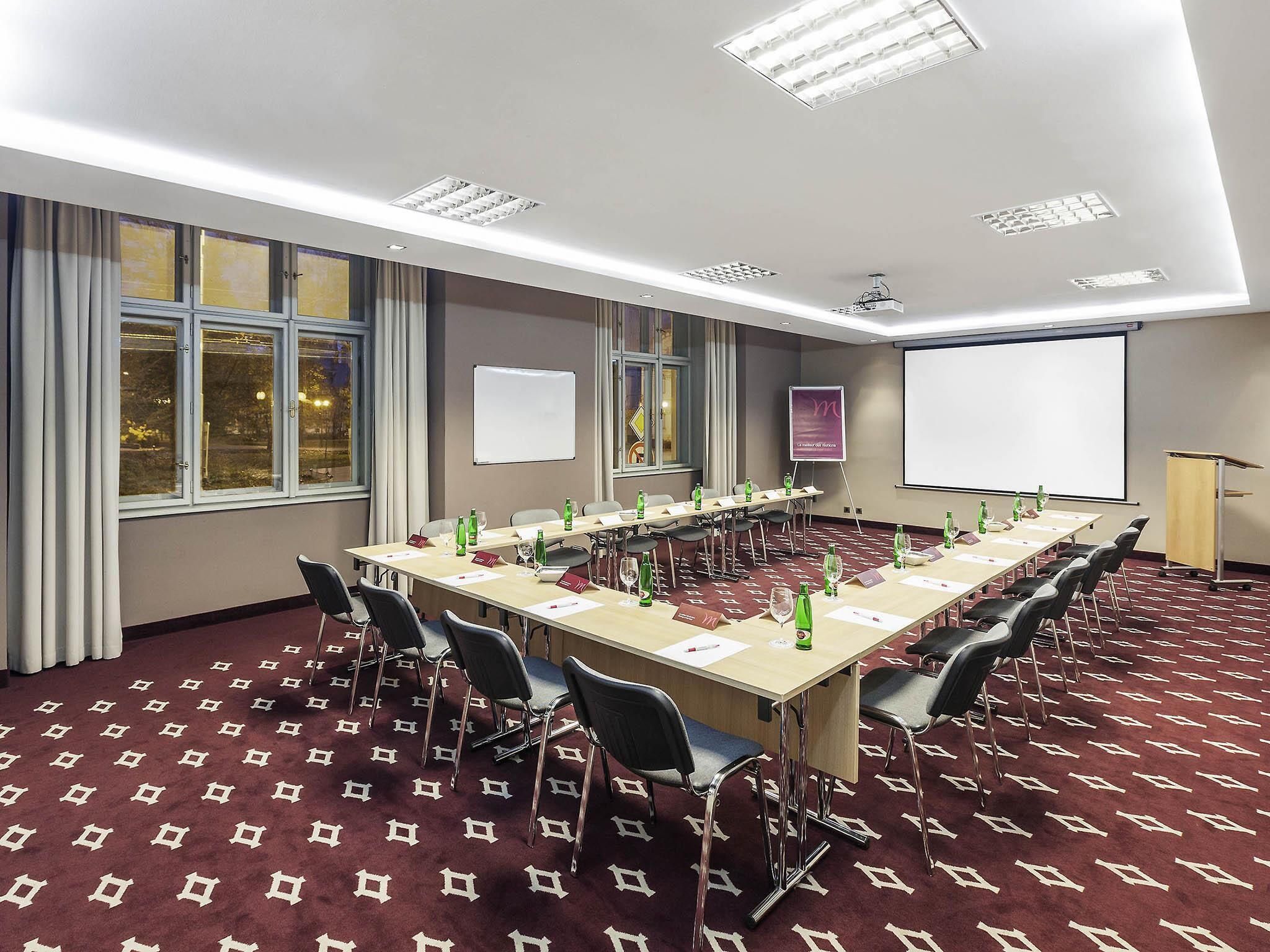 Uma sala de conferência com uma mesa comprida, cadeiras, uma tela de projetor e um quadro branco.
