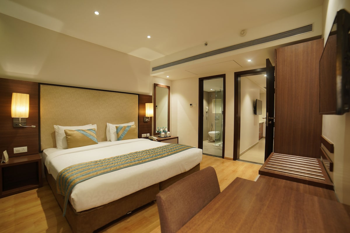 Quarto de hotel com cama grande, mesas de cabeceira, escrivaninha e chuveiro.