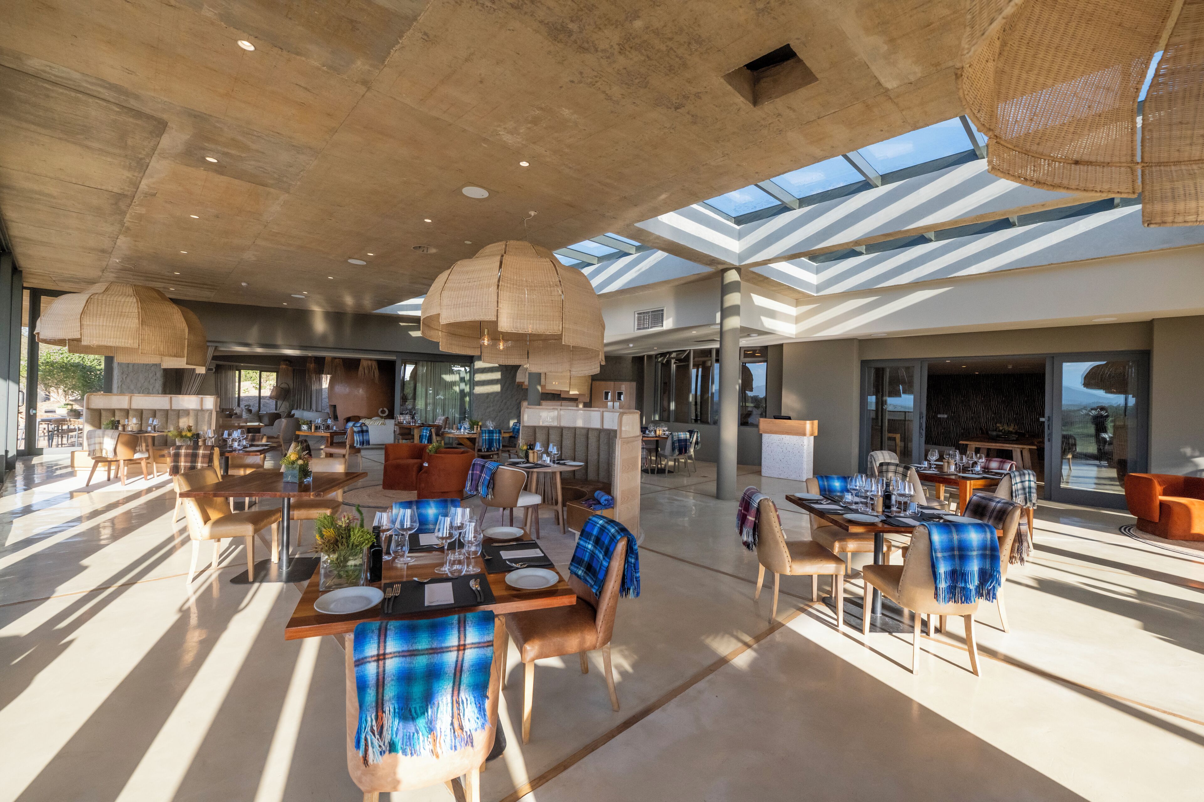 Uma sala de jantar ampla, com pé direito alto, grandes janelas e móveis modernos.