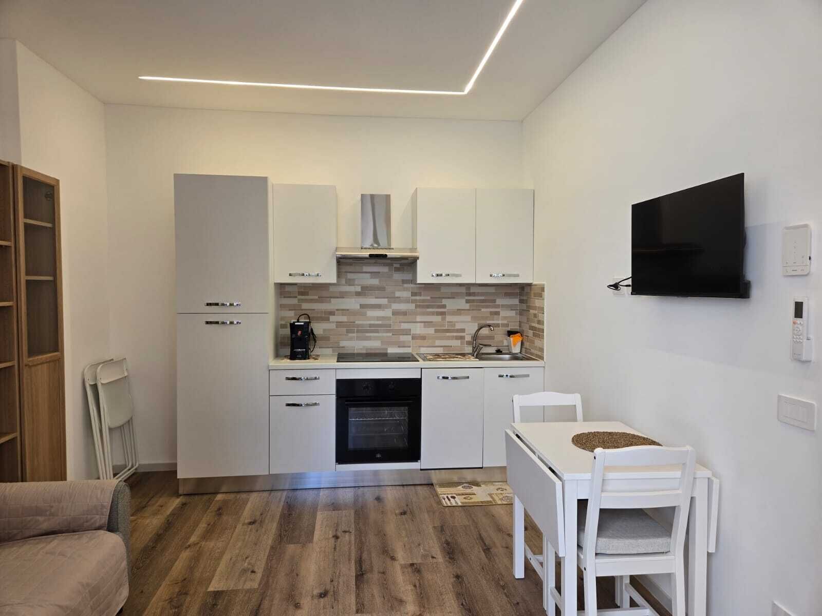 Uma cozinha compacta com armários brancos, micro-ondas e um pequeno espaço de refeições com mesa e cadeiras.