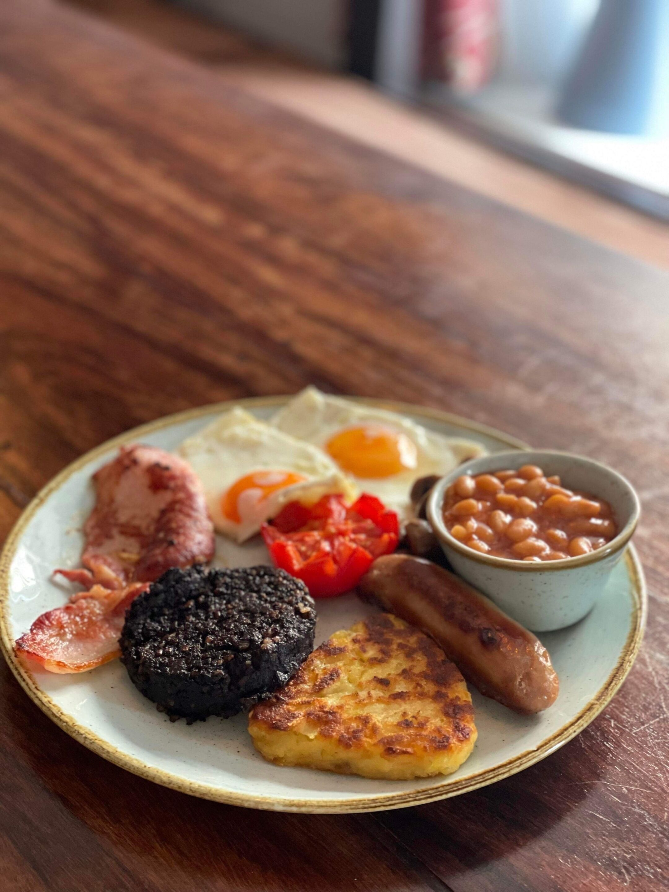 Prato de comida de café da manhã com ovos, linguiça, bacon, morcela, feijão cozido e batata frita.
