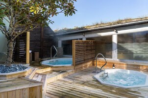Um deck de madeira com duas banheiras de hidromassagem, uma árvore e uma área envidraçada com vista.