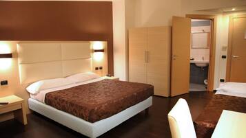 Quarto de hotel com cama grande, mesas de cabeceira, guarda-roupa, banheiro com espelho e pia, e uma cadeira.