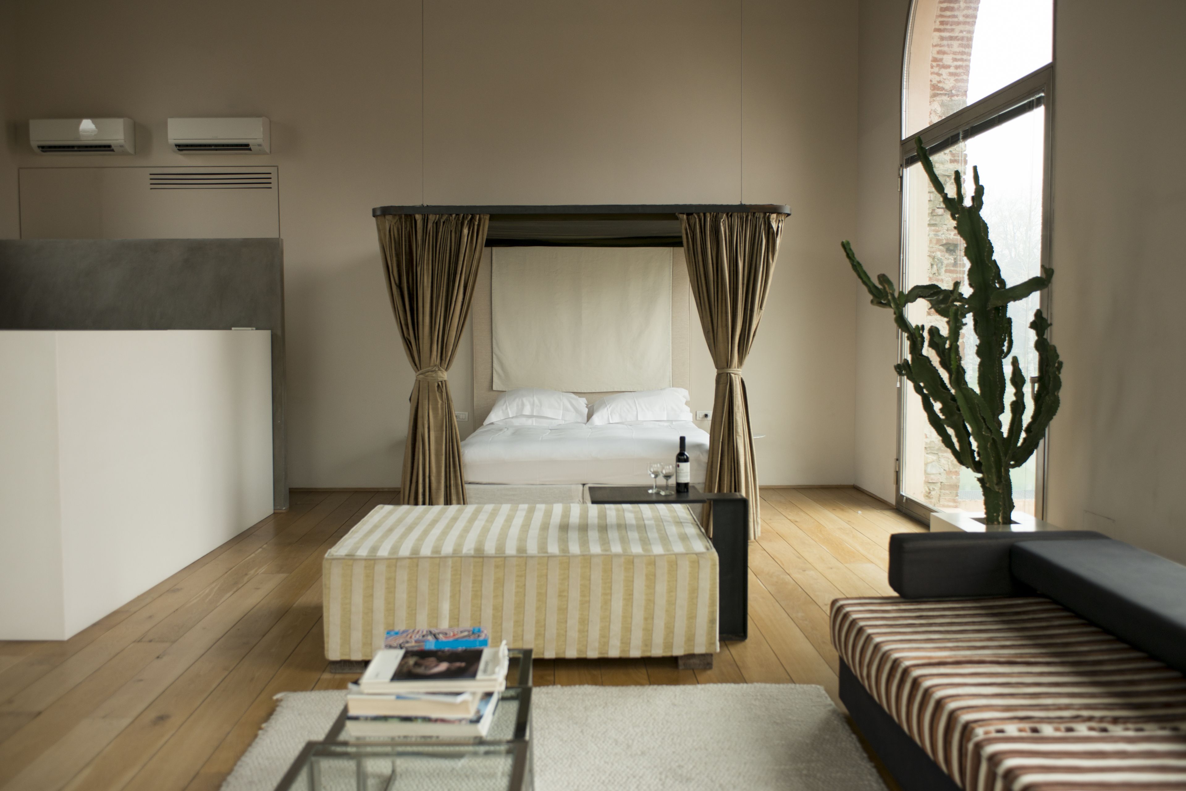 Quarto moderno com cama, mesa de cabeceira e uma grande janela com vista para um cacto.