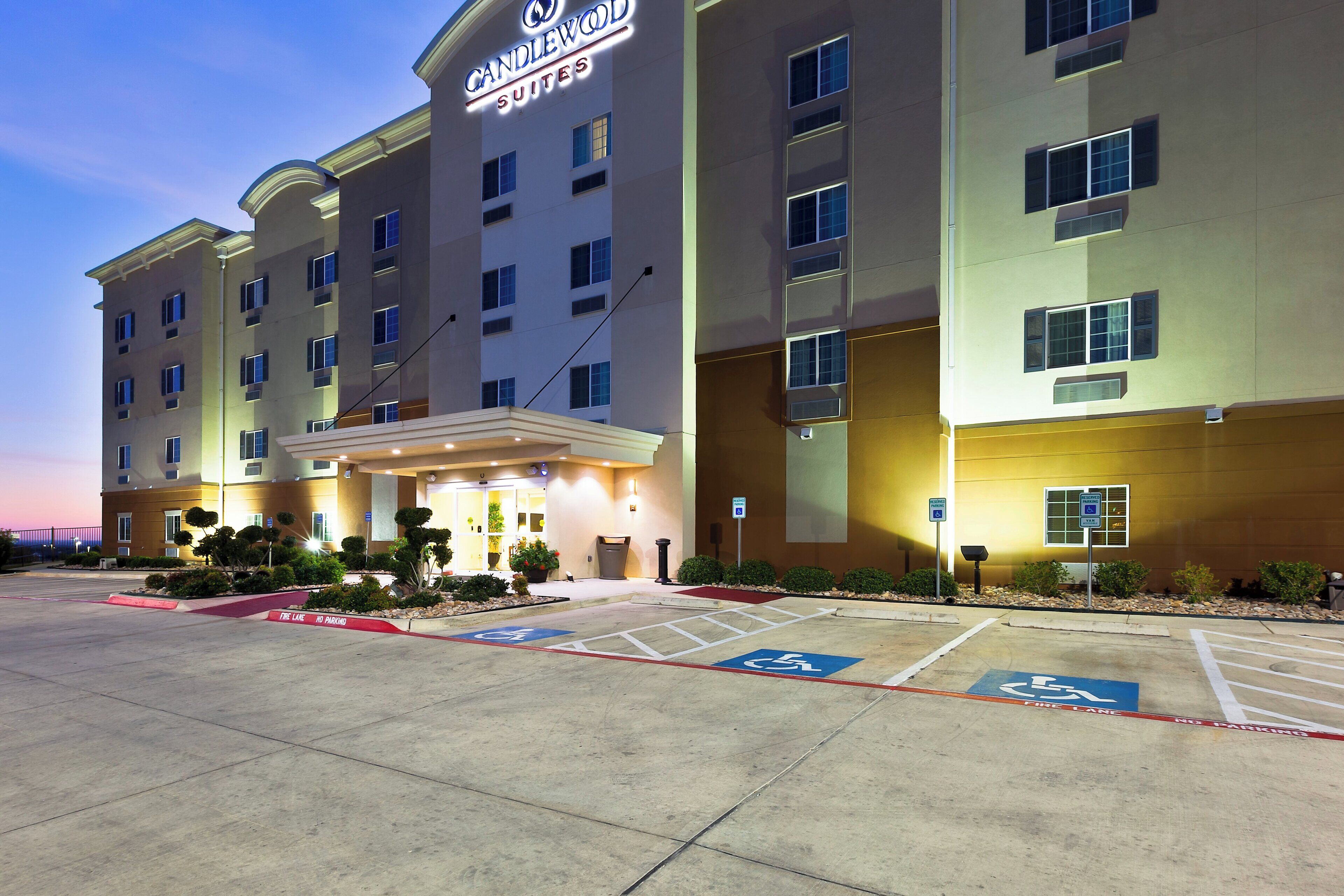 Um hotel com uma placa indicando 'CANDLEWOOD SUITES' e um estacionamento com vagas reservadas para deficientes.