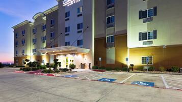 Um hotel com uma placa indicando 'CANDLEWOOD SUITES' e um estacionamento com vagas reservadas para deficientes.