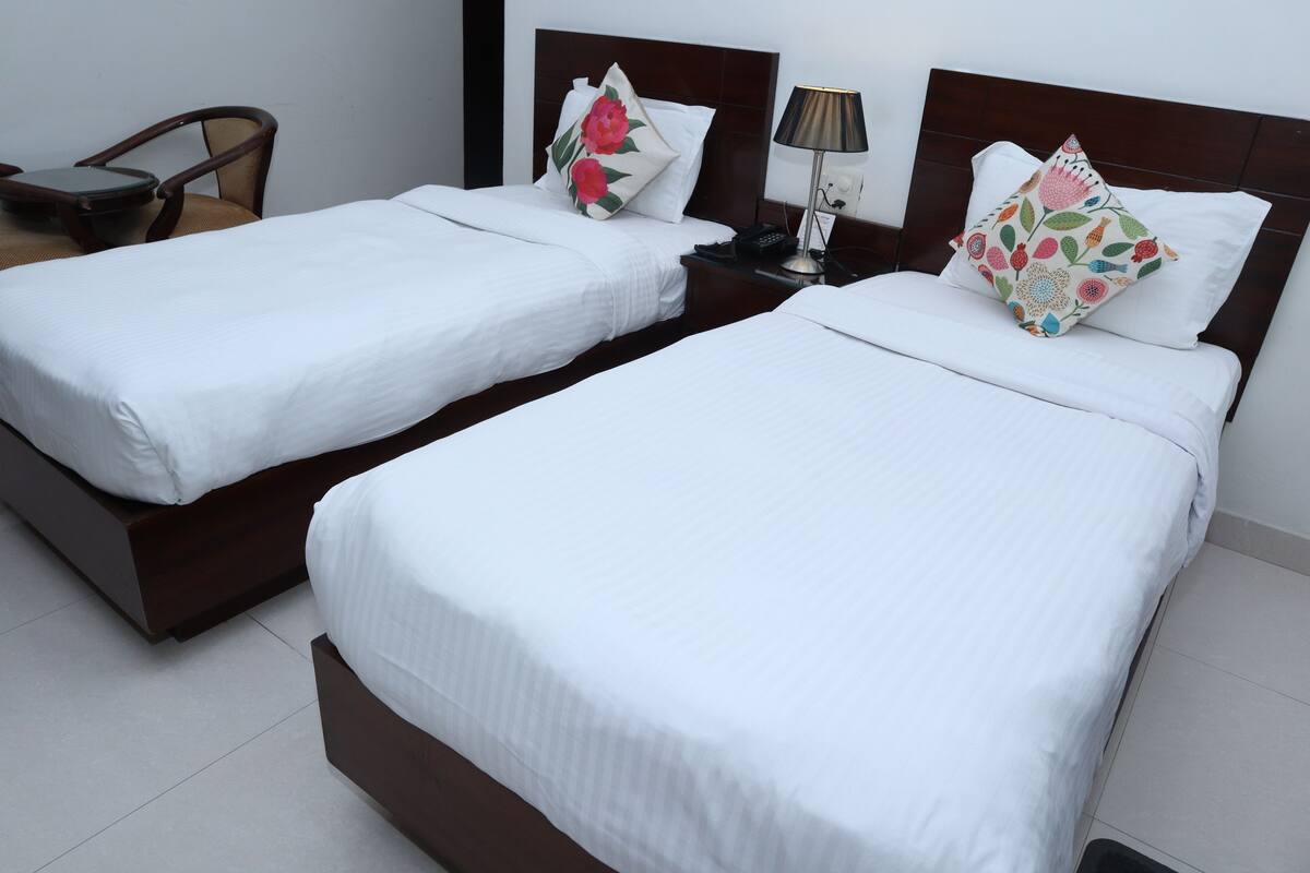 Duas camas de solteiro com cabeceiras de madeira, roupa de cama branca e almofadas com padrão floral.