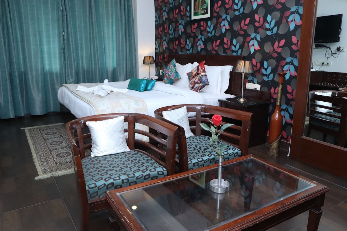 Quarto de hotel com cama, duas cadeiras de madeira, mesa de centro de vidro, televisão e parede estampada.