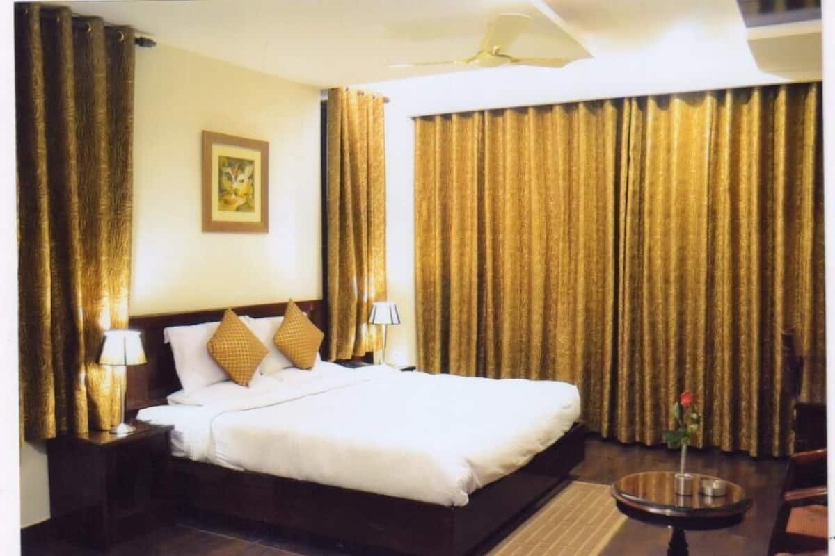 Quarto de hotel com uma cama grande, duas mesas de cabeceira com abajures, um quadro na parede e uma mesa redonda com um vaso.