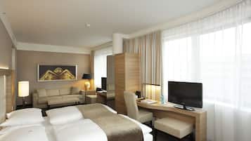 Quarto de hotel com uma cama grande, uma escrivaninha com computador, uma cadeira, televisão e um sofá.