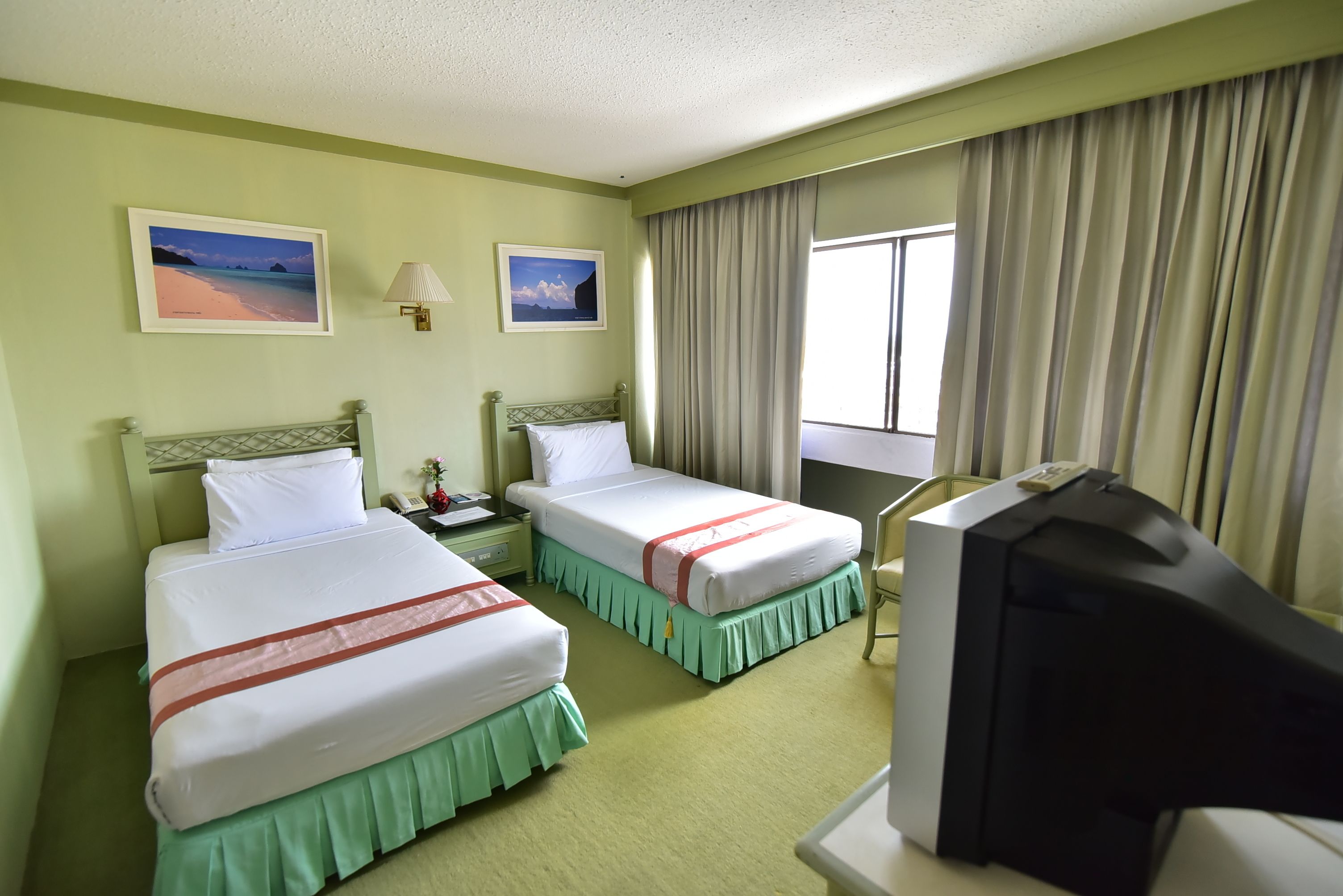 Quarto de hotel com duas camas, uma televisão, um abajur e duas imagens emolduradas na parede.