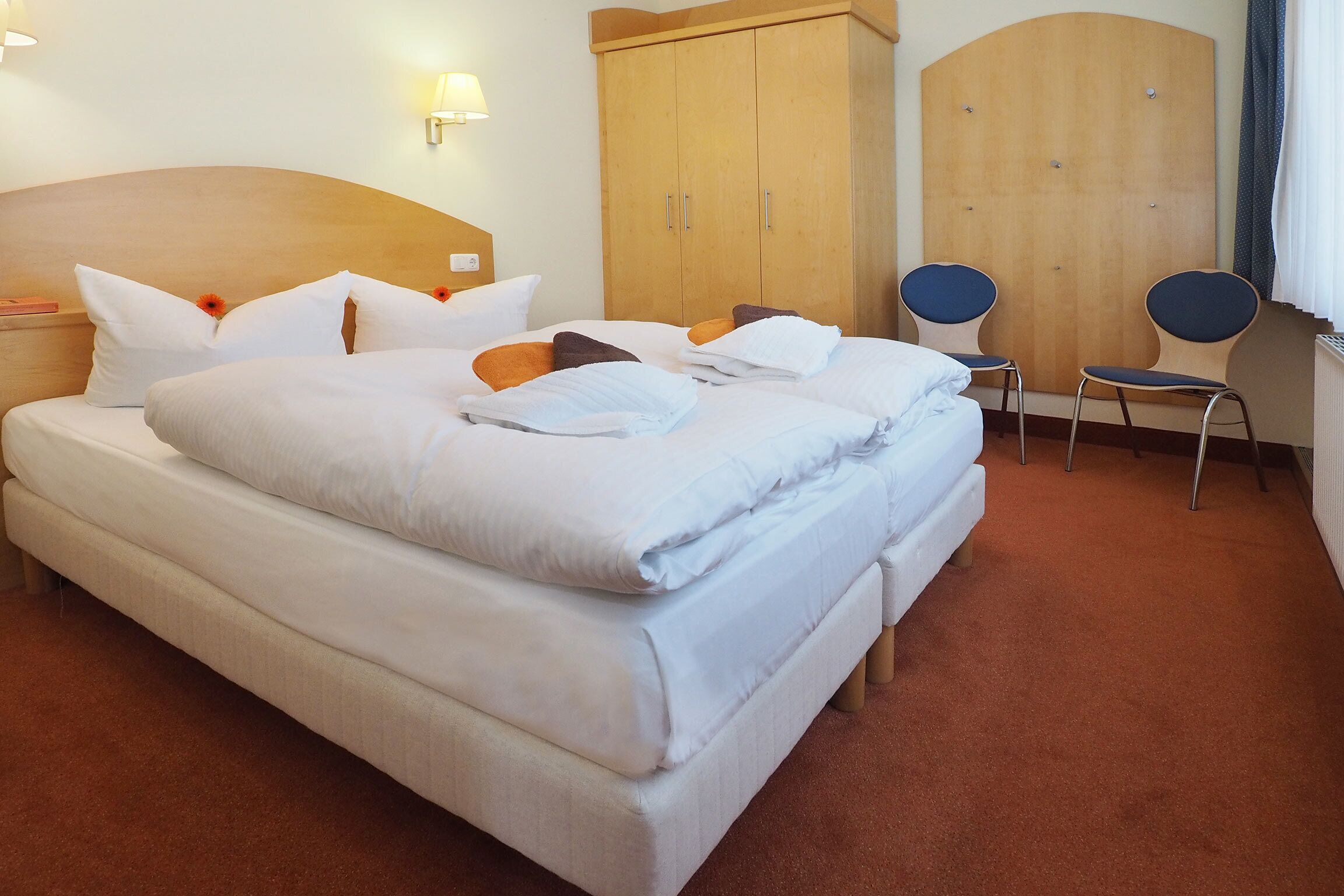 Quarto de hotel com uma cama grande, duas cadeiras, um guarda-roupa e uma mesa de cabeceira.