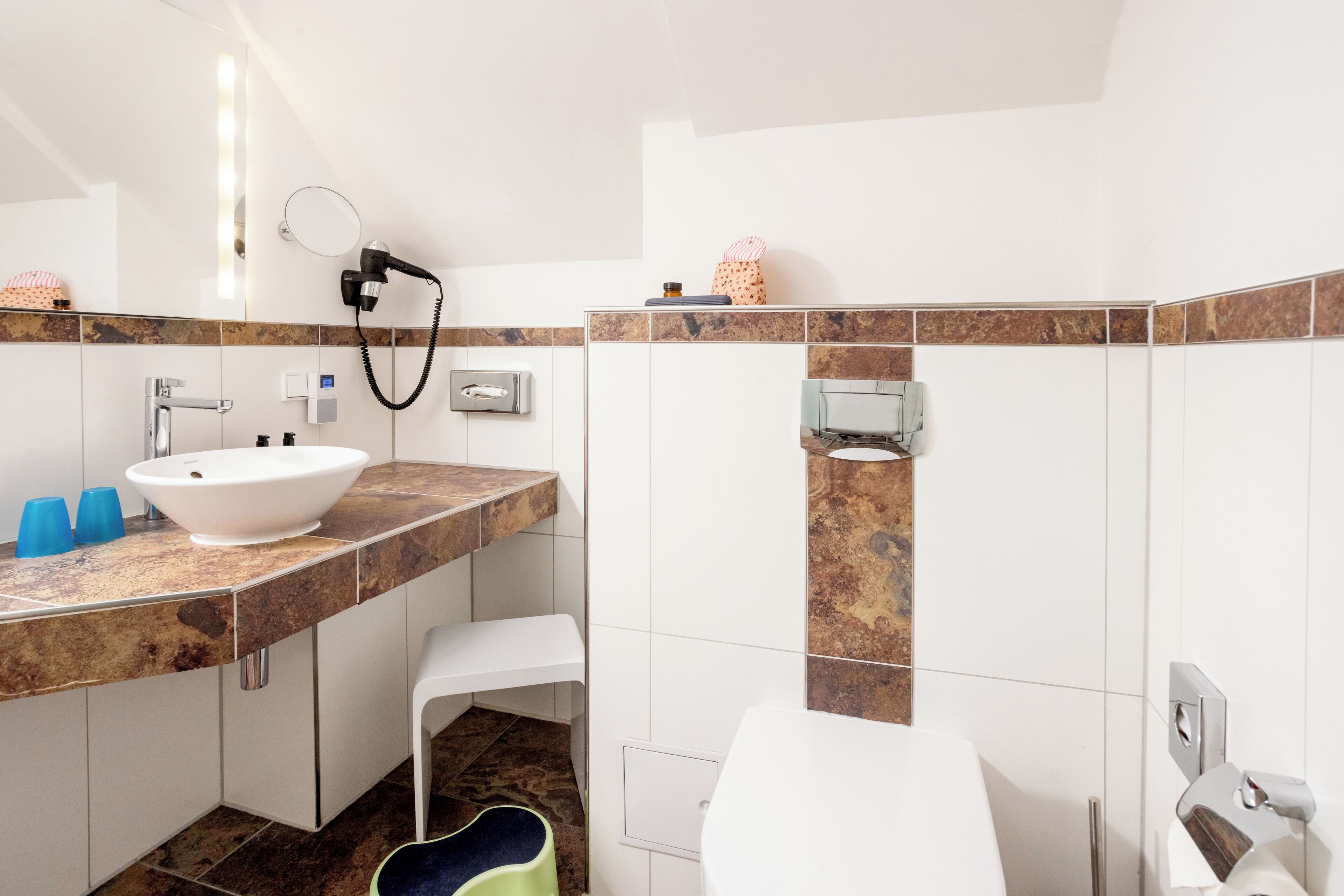 Casa de banho com lavatório branco, secador de cabelo, suporte para toalhas e sanita.