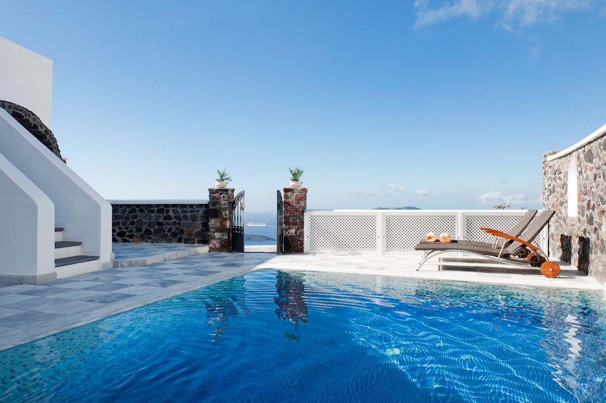 Uma piscina infinita no terraço com vista clara para o mar, uma espreguiçadeira e um muro de pedra.