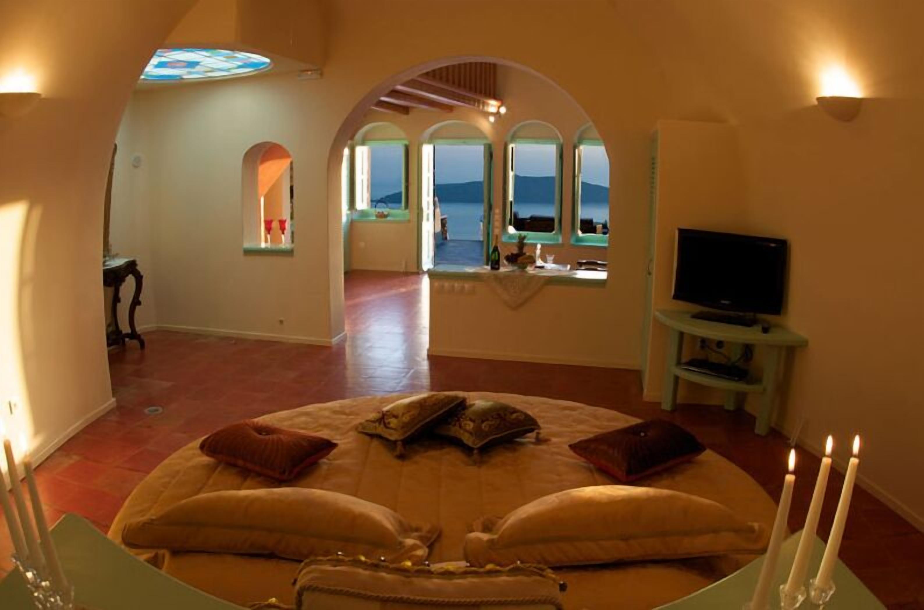 Quarto com cama grande, televisão e vista para o mar através de janelas em arco.