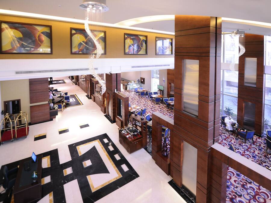 Um saguão de hotel com escadaria central, áreas de estar e obras de arte nas paredes.