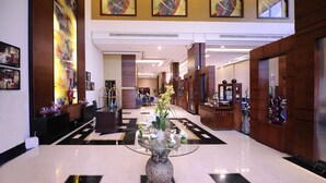 Um saguão de hotel com uma mesa redonda central, uma recepção e um balcão de check-in.