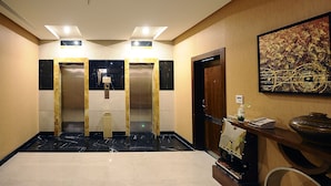 Um saguão de hotel com dois elevadores, um balcão de recepção e um vaso grande à direita.