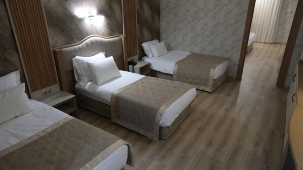 Quarto de hotel com duas camas de solteiro, uma mesa de cabeceira, uma luminária e piso de madeira.