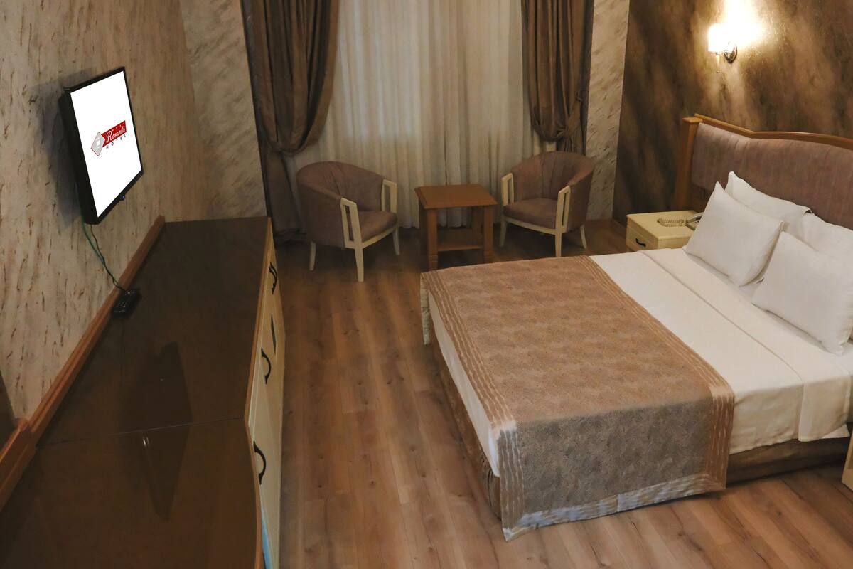 Quarto de hotel com cama, mesa de cabeceira, cadeira e uma pequena mesa.